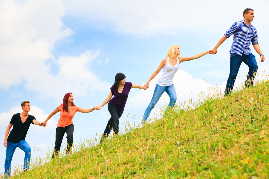 young people helping each other climb a hill – Adult Christian Formation